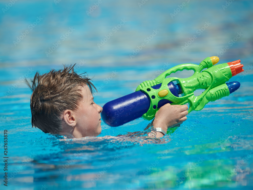 Cute boy is shooting from the water gun in the swimming pool, he is on ...