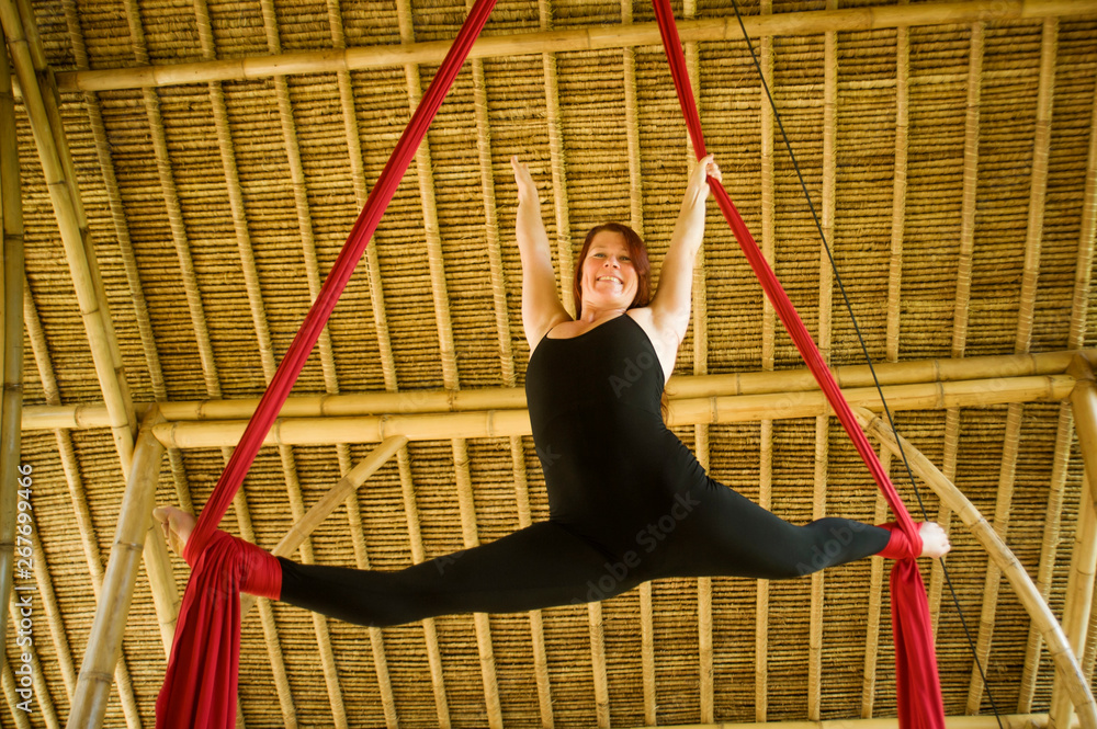 attractive and athletic aerialist woman hanging from silk fabric doing ...