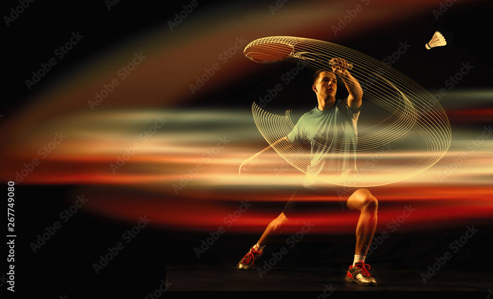 Young man playing badminton over dark studio background. Male athlete ...