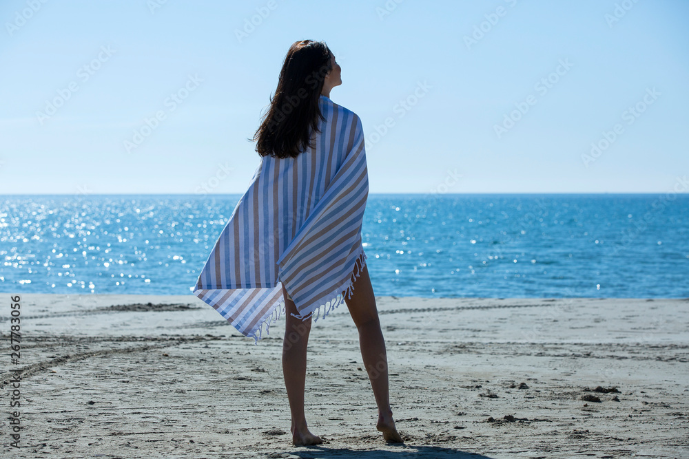 Pretty young girl wrapped in beach towel poses to camera. Full length ...