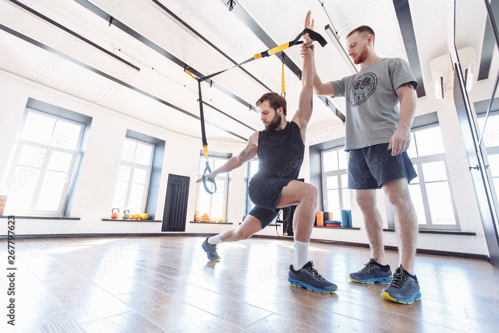 Male trainer teaches his student how to workout with suspended training ...