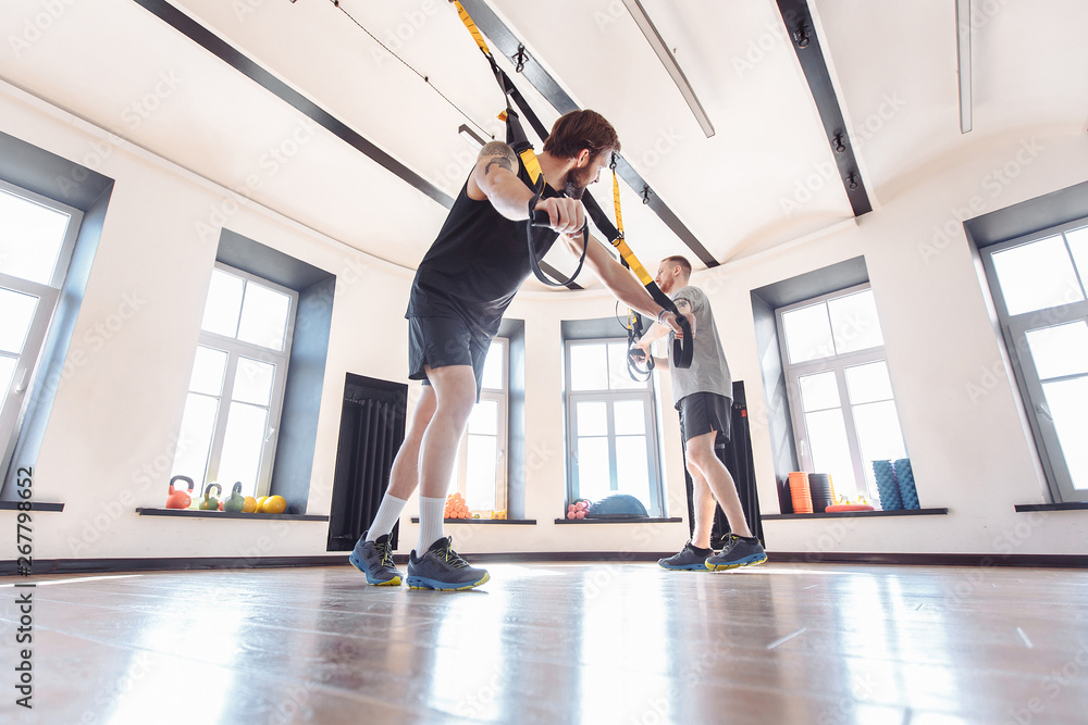 Positive young men athletes work out together in the gym using hanging ...