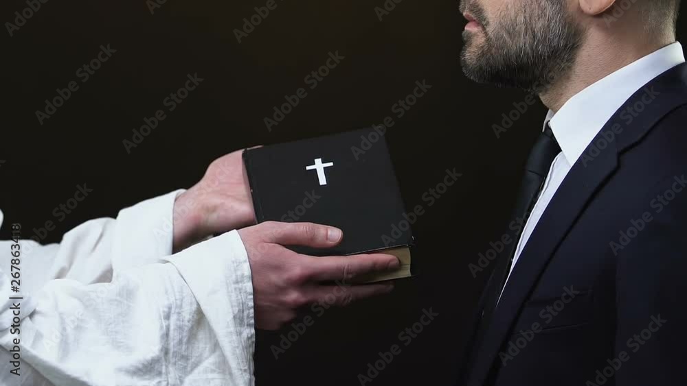 Priest giving business man holy bible against black background ...