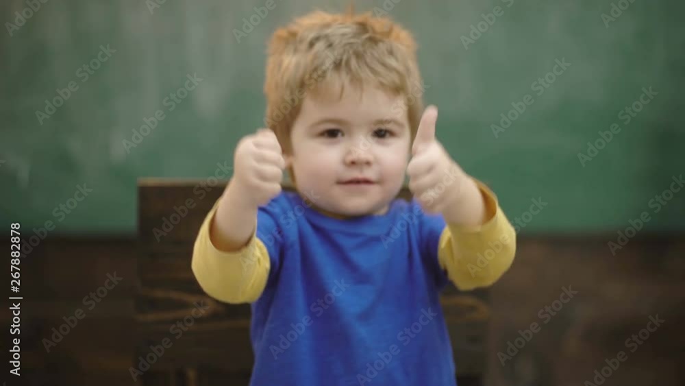 Boy raises his thumb up against background of a green school board ...