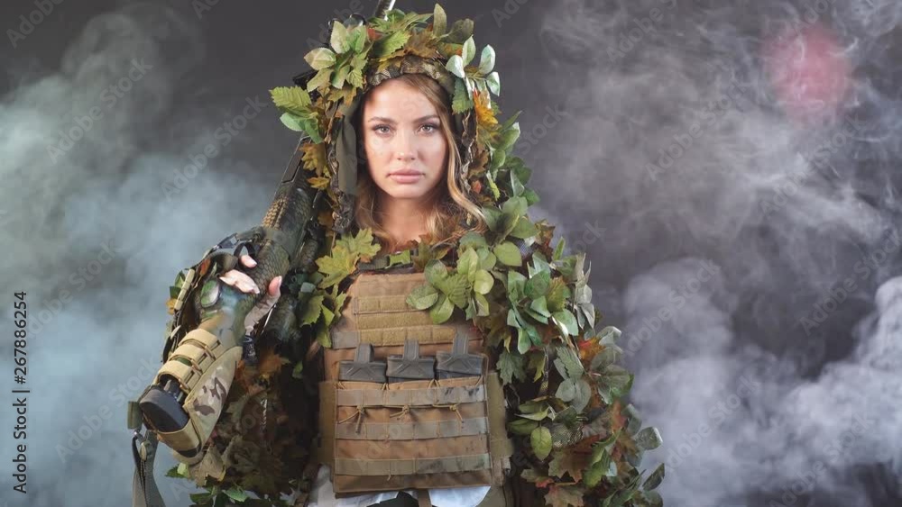 Heavily armed female soldier in battle helmet and ghillie suit holding ...