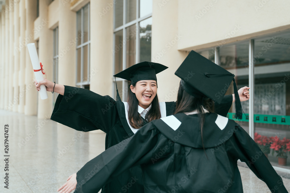 Two young student girls dressed in black graduation gown smiling ...