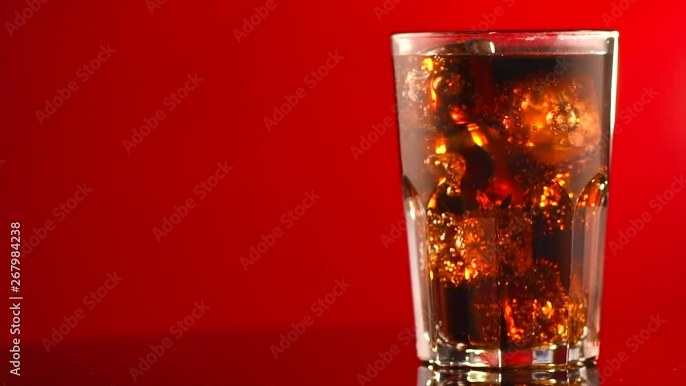 Coke with ice cubes closeup. Glass of fizzy cola rotated over red ...