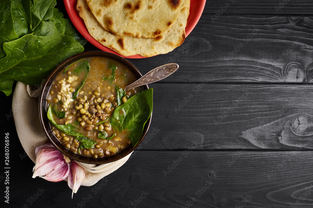 Mung Dhal with Spinach, Chapati and garlic at black wooden tabletop ...