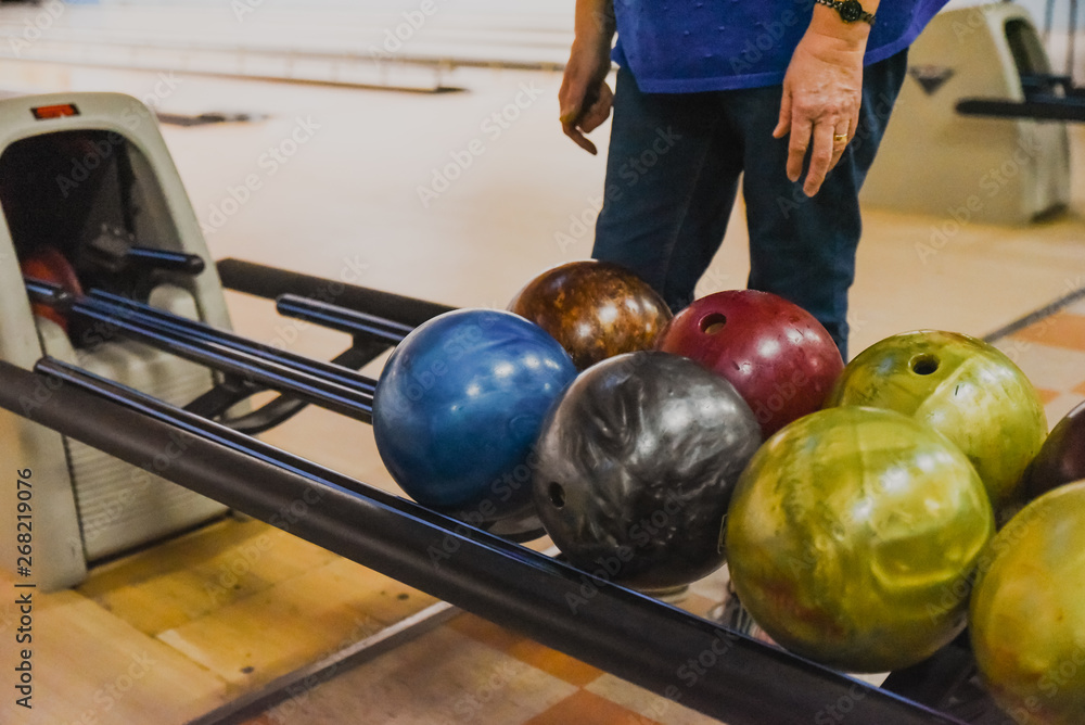 Cropped image of older woman standing behind rows of bowling balls ...