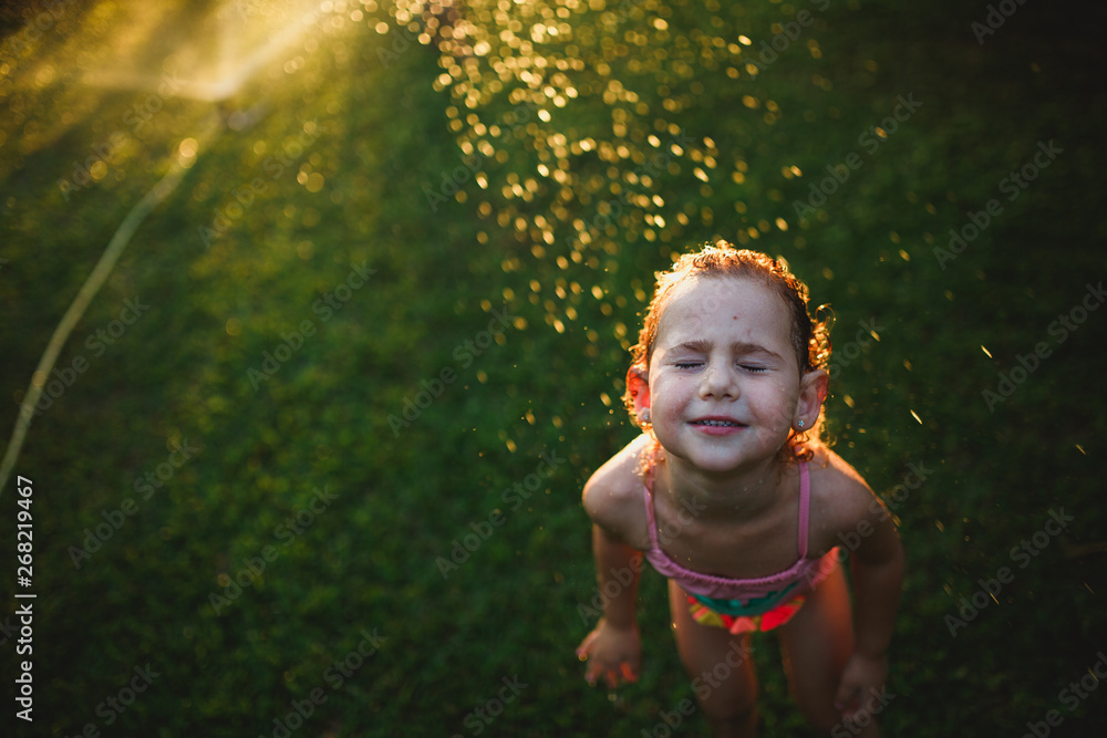 Girl in swimsuit playing on grass with sprinkler Stock Photo | Adobe Stock