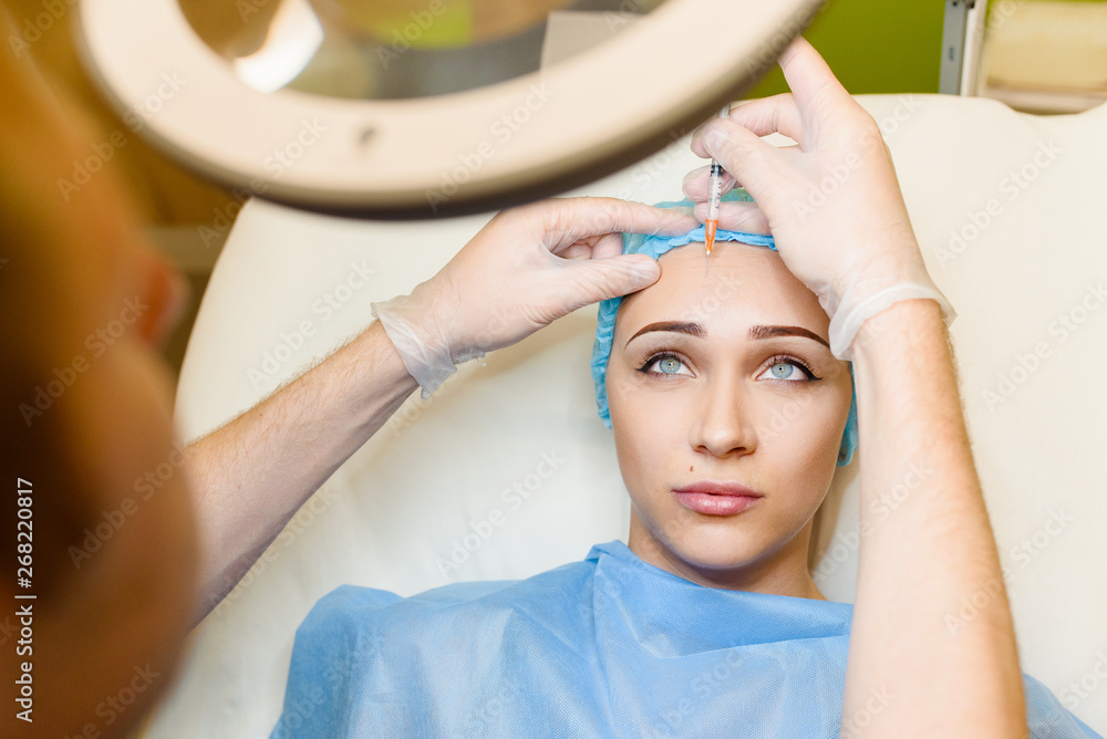 Woman makes botox injections in forehead area. Doctor cleans the girl's ...