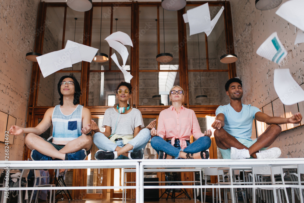 Relaxed students in glasses sitting in lotus pose in library while ...