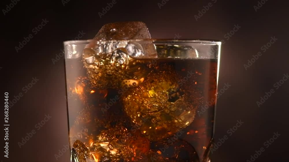 Coke with ice cubes closeup. Glass of fizzy cola rotated over brown ...