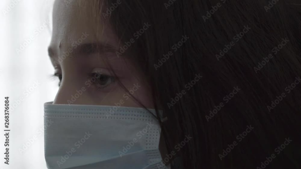 Close up portrait sad sick girl with a sterile mask on her face looking ...