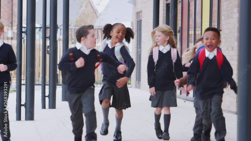 Happy primary school kids in uniforms running on a walkway outside ...