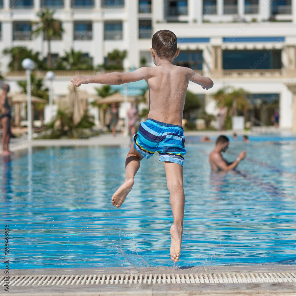 European boy jumping into swimming pool at resort. Moment of taking off ...