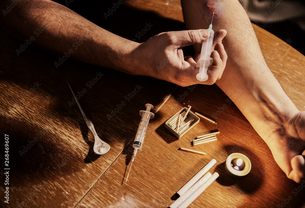 Man shooting heroin with needle syringe. Drugs addict. Candle burning ...