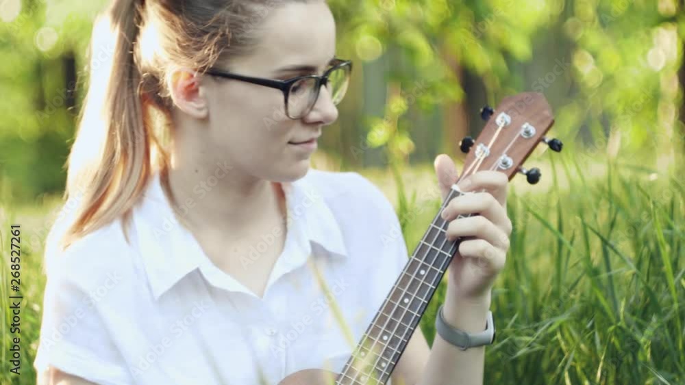 Young beautiful girl playing the ukulele. Funny Caucasian girl playing ...
