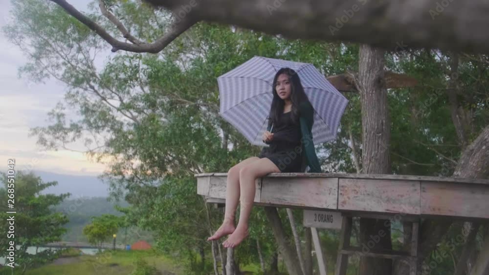 Lone girl sitting on wooden deck holding an umbrella and dangling her ...