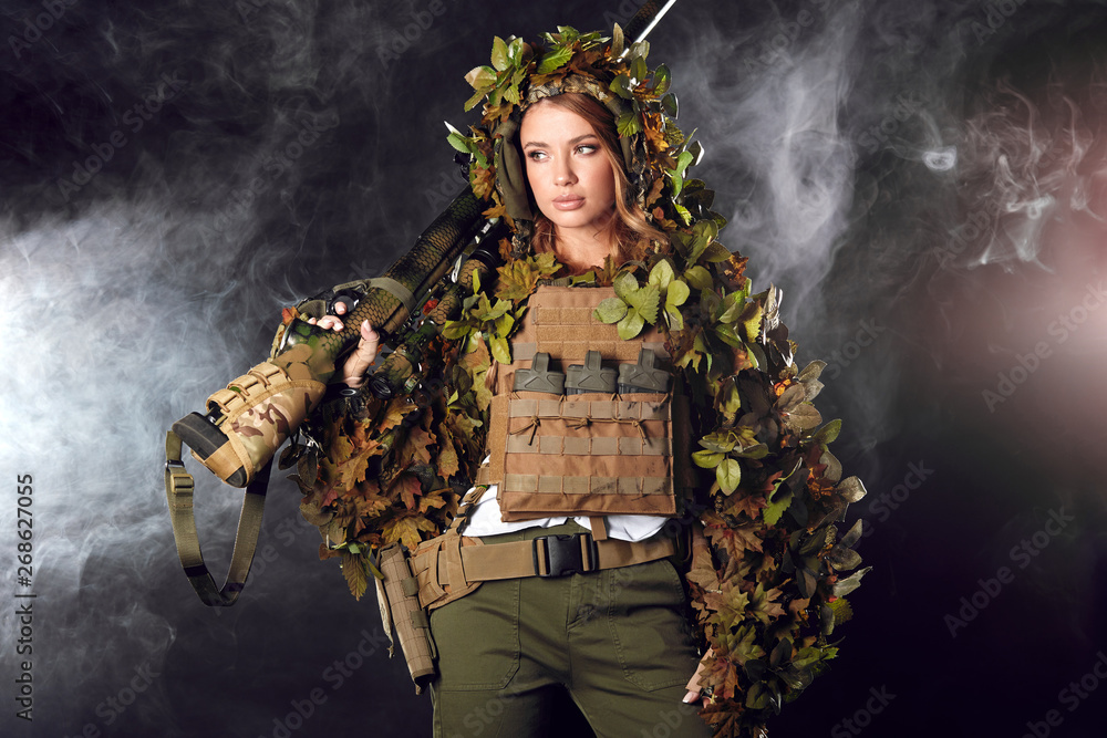 Heavily armed female soldier in battle helmet and ghillie suit holding ...