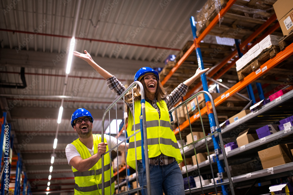 Warehouse workers having fun at work. Happy people pushing carts while ...