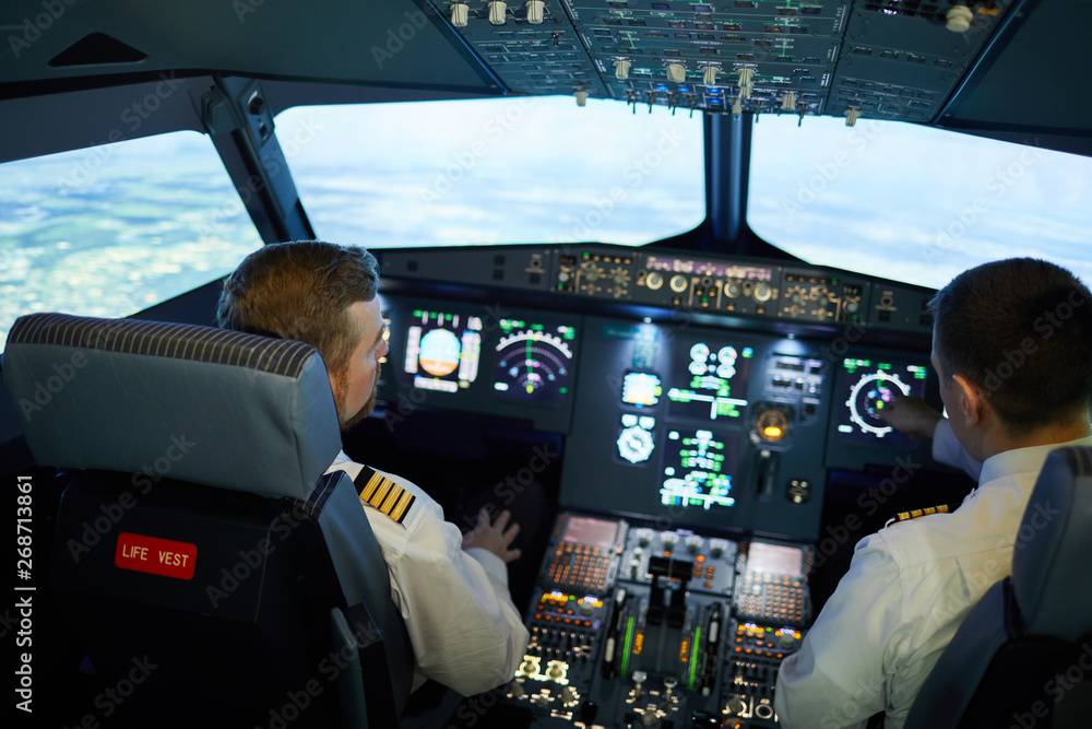 Rear view of modern pilots in uniform with stripes sitting in armchairs ...