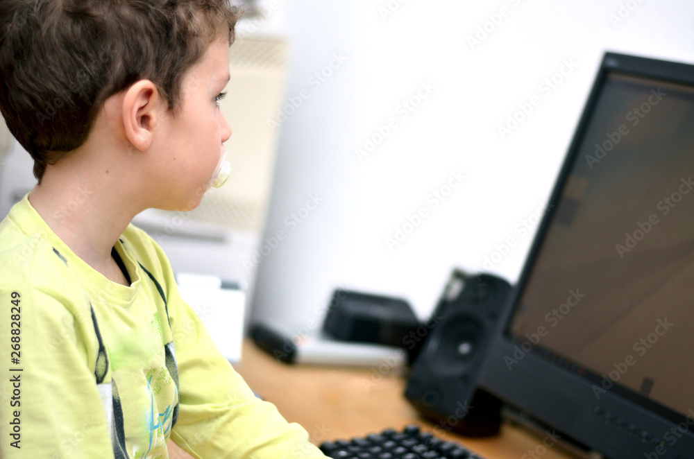 Kind sitzt vor einem Computer mit Nuckel im Mund Stock Photo | Adobe Stock