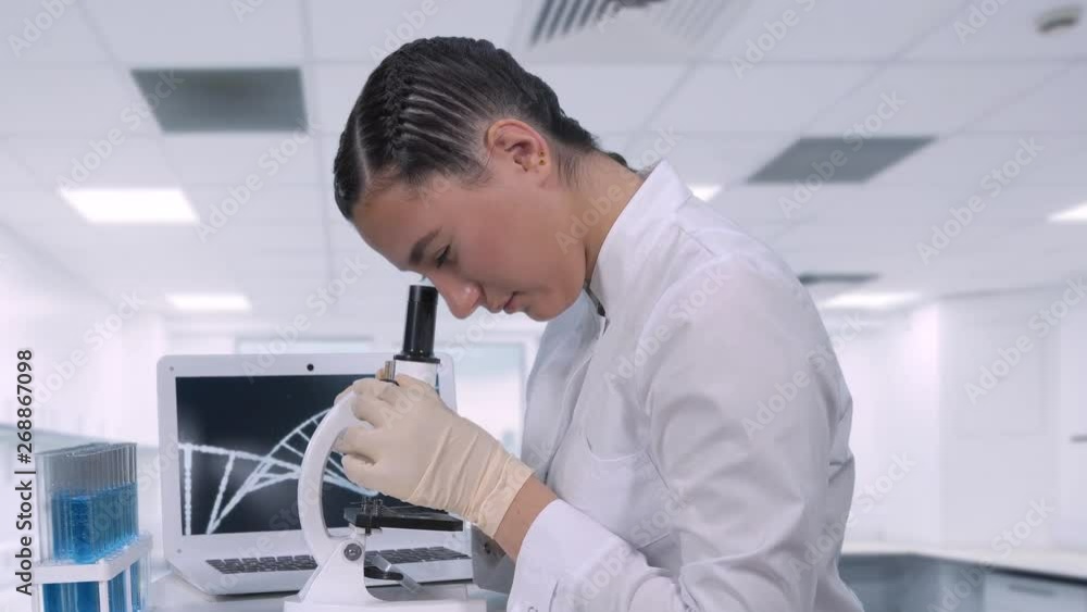 A female lab technician sitting at a table next to a laptop in a ...