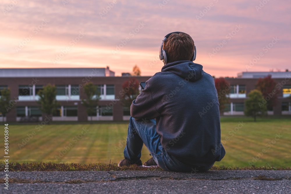 Foto de Teenager sitting alone at the top of a hill at sunset. He is ...