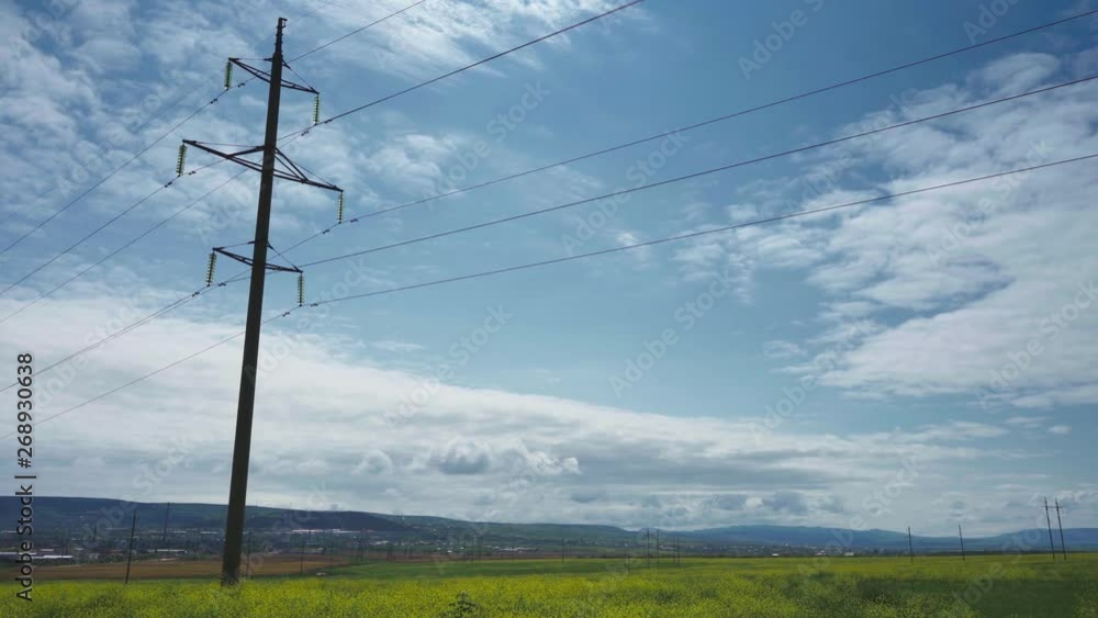 Huge high voltage electric pylon in a green field with yellow flowers ...