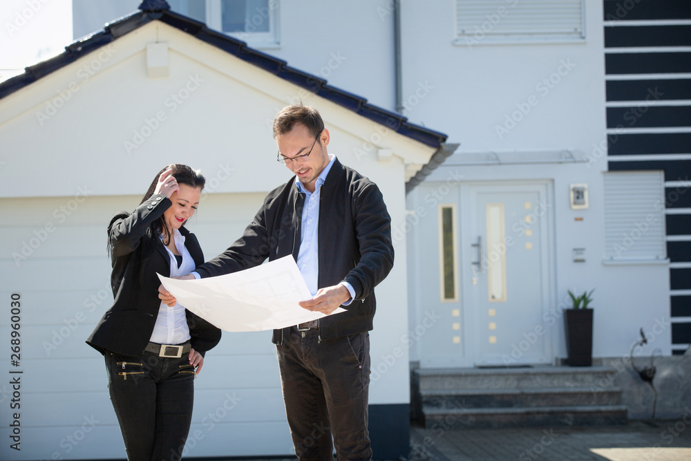 A real estate agent showing a customer house plan in front of the house ...
