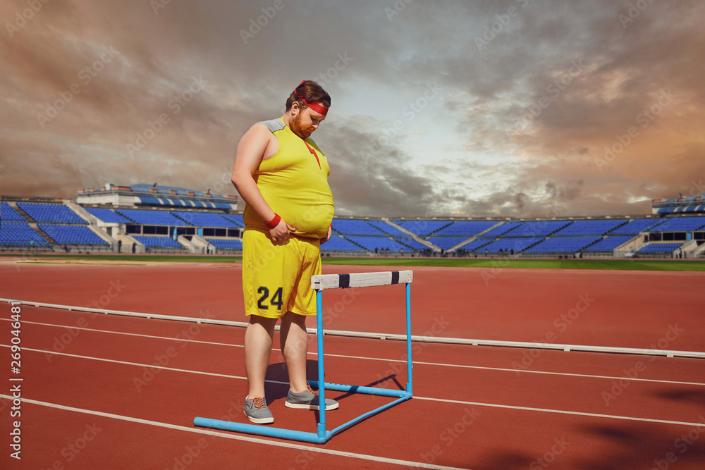 Fat man in sportswear stands in front of a barrier on a track stadium ...