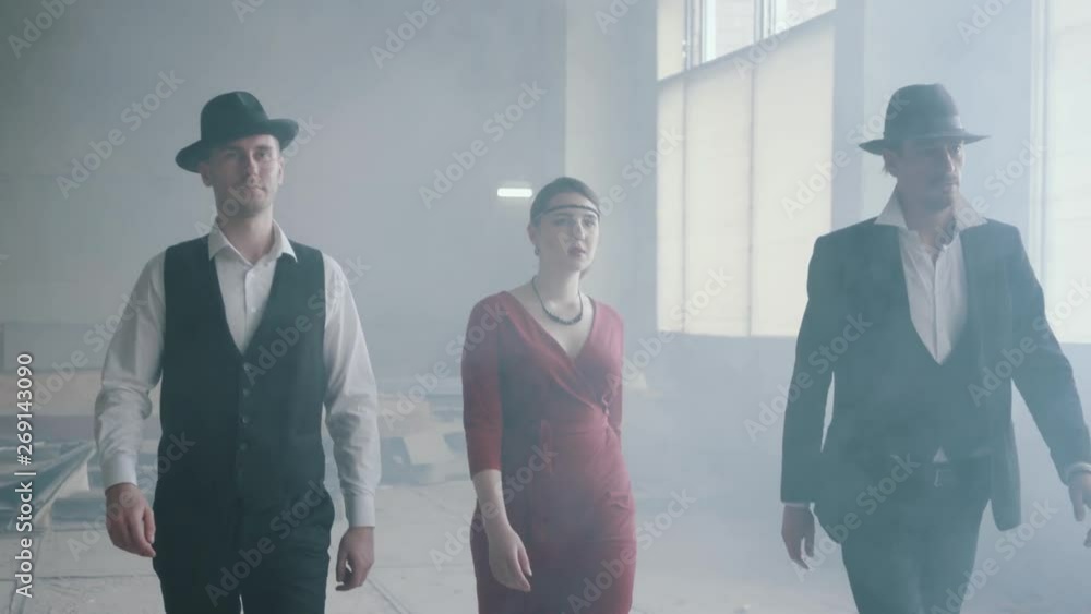 Two confident men in hats and suits and woman in red dress walking ...
