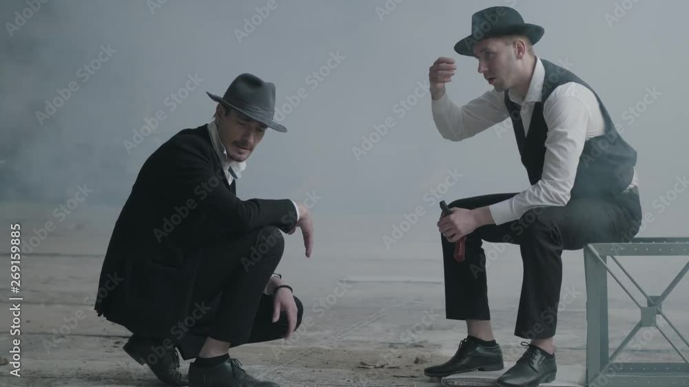 Two stylish men in hats, one sitting on the chair, another squatting in ...