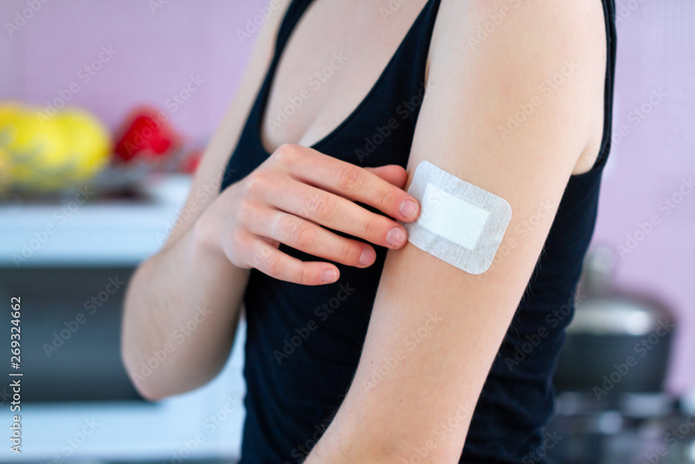 Woman using a medical adhesive bandage on arm after vaccination ...