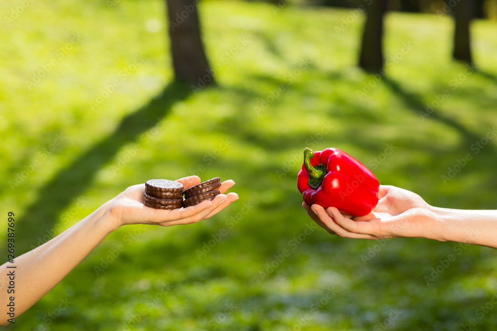 Two hands, female and male, holding and comparing cookie and red pepper ...