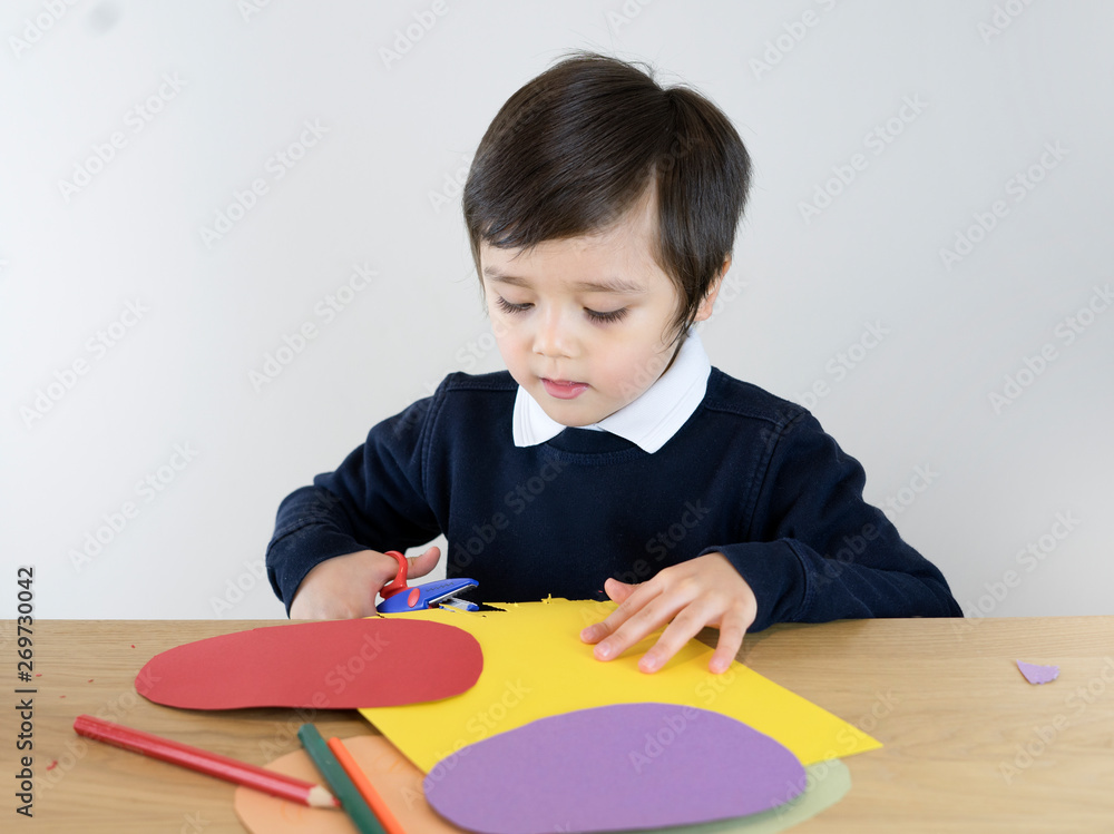 Foto de Child cutting colore paper with scissors at the table, Portrait ...