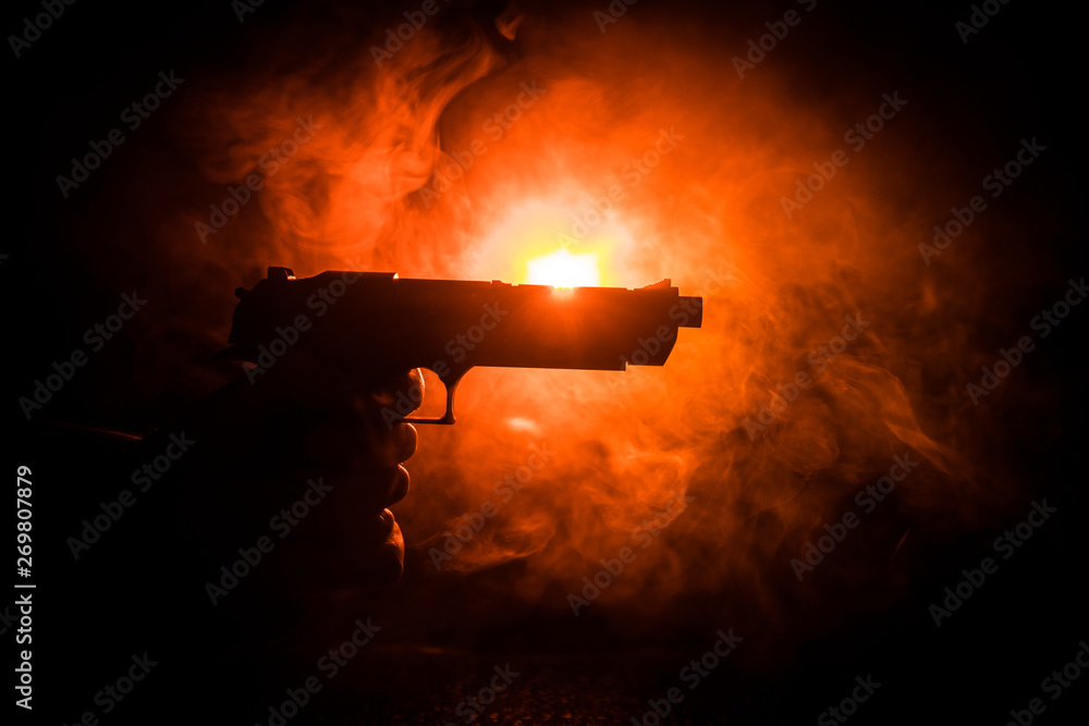 Male hand holding gun on black background with smoke toned back lights ...