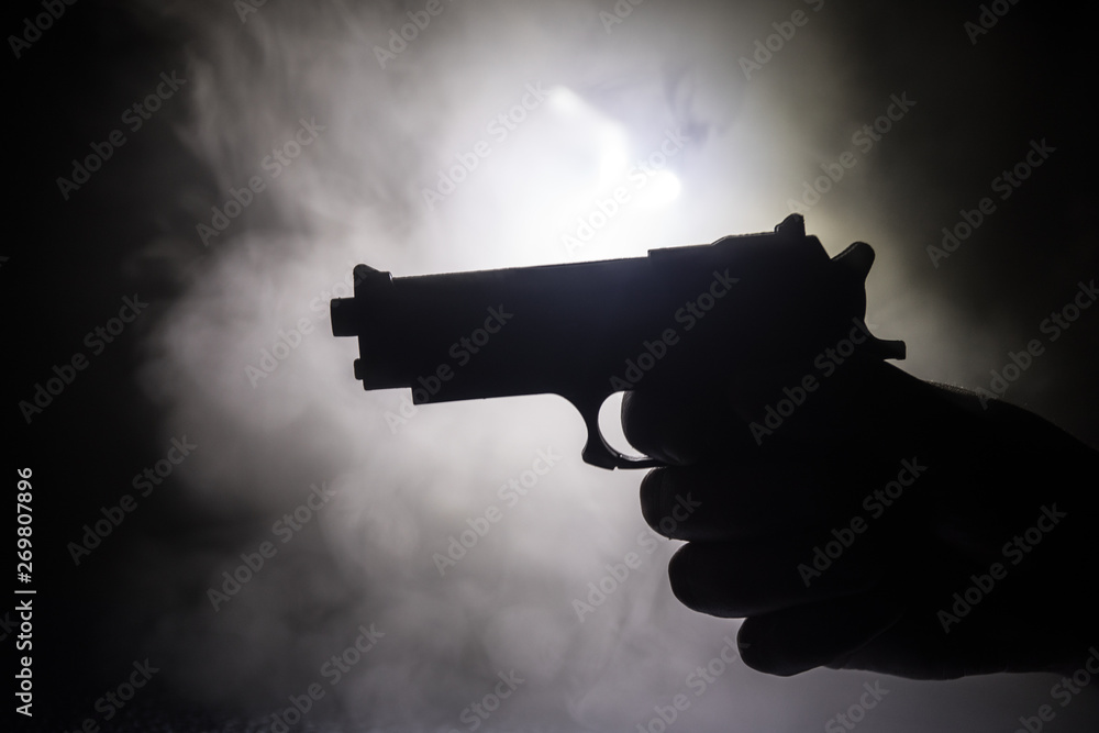 Male hand holding gun on black background with smoke toned back lights ...