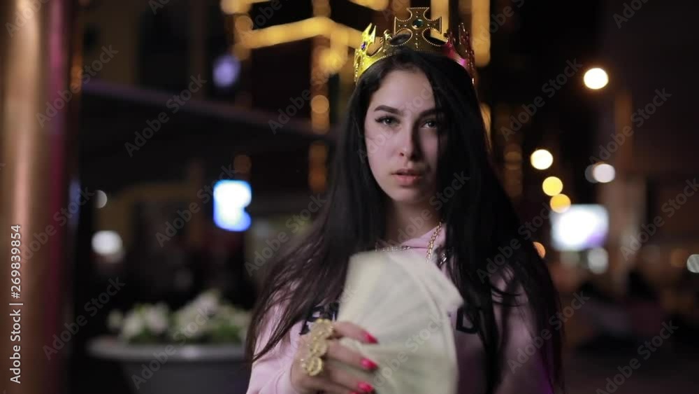 Rich girl in crown like queen cooling her face with fan of money at ...