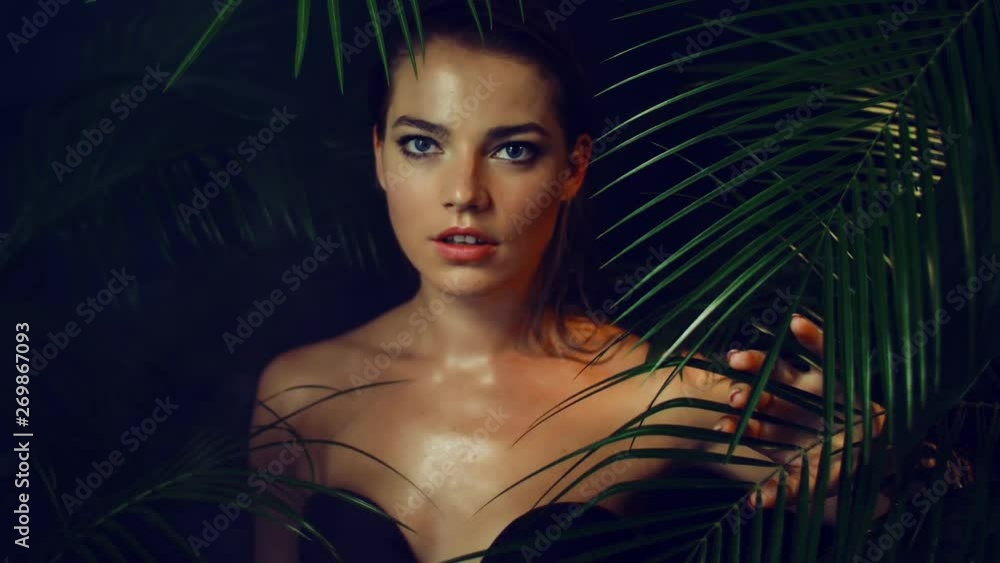 Beautiful girl with tanned skin poses and walks among tropical plants ...