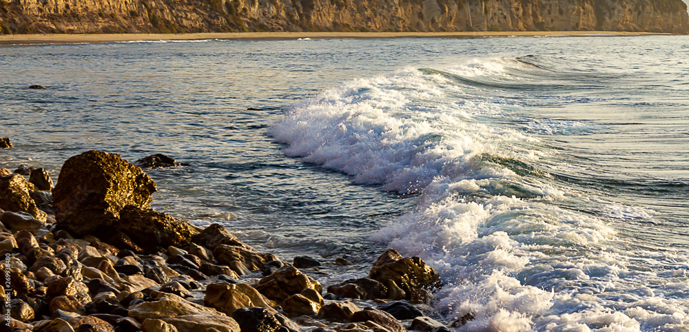pastel colored foam rolling infront of wave towards rocky shore with ...