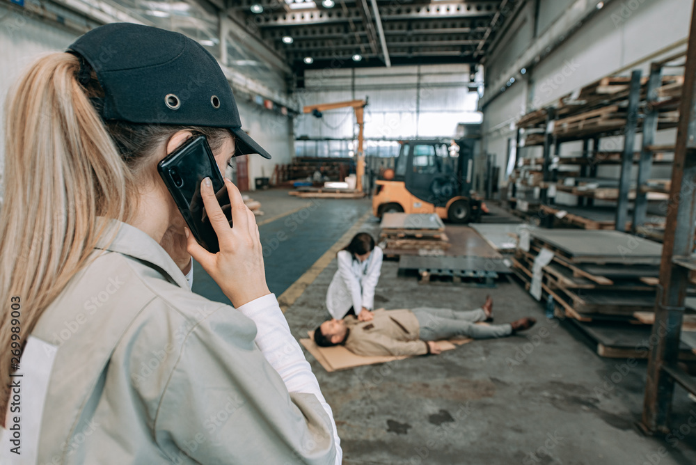 Female factory worker calling ambulance while doctor giving CPR to a ...