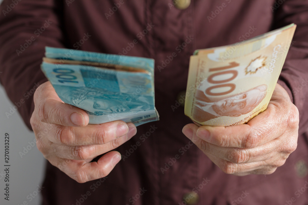 Canadian Dollars and Brazilian currency. Front view of old woman's hand ...