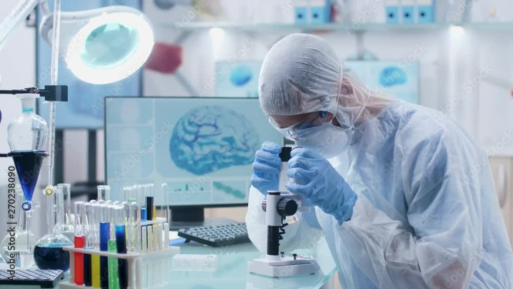 Researcher working in professional laboratory, looking at microscope ...