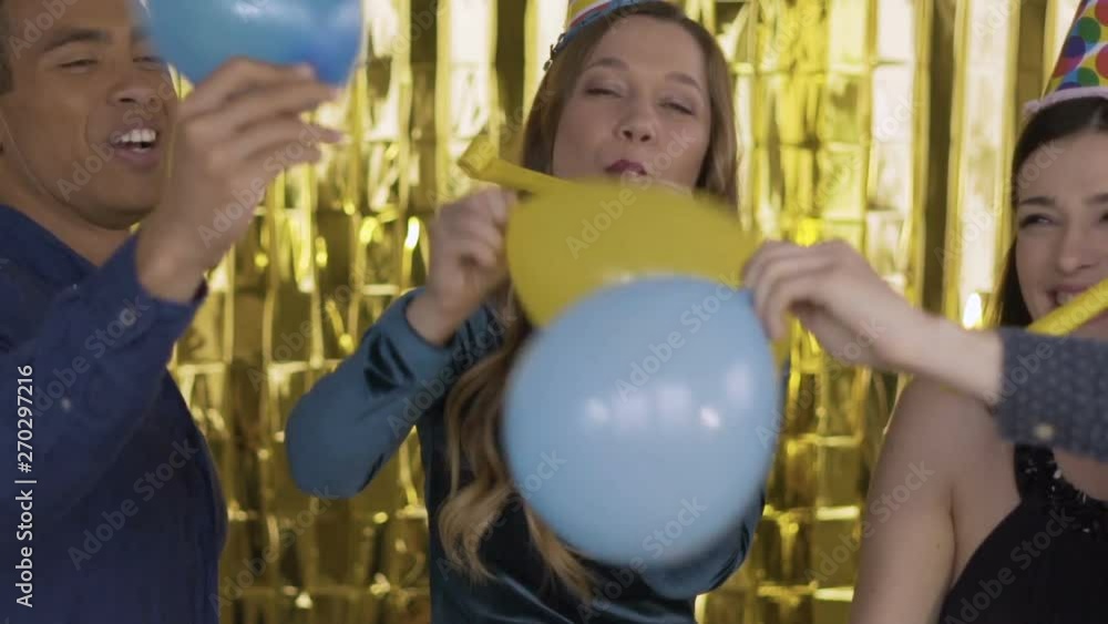 4 happy cheerful people at a party in paper caps fighting balloons. The ...
