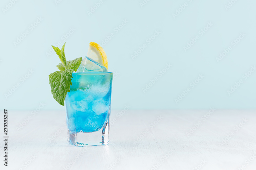 Summer fresh blue curacao cocktail with lemon slice, ice cubes, mint in wet shot glass on white ...