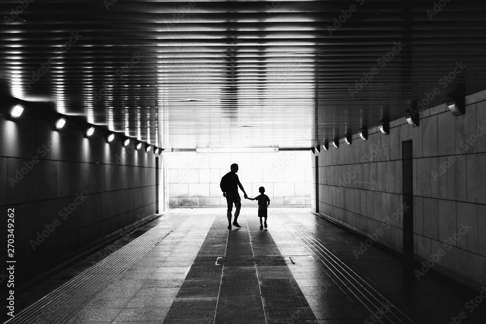 Silhouettes in the tunnel - man and little child walking through empty ...