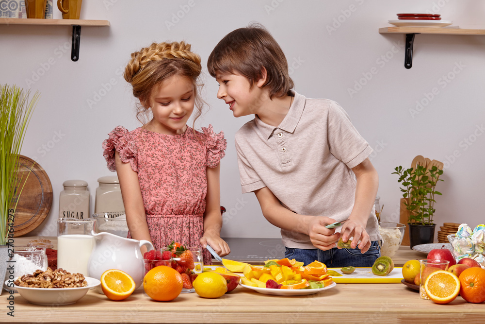 Cute kids are cooking together in a kitchen against a white wall with ...
