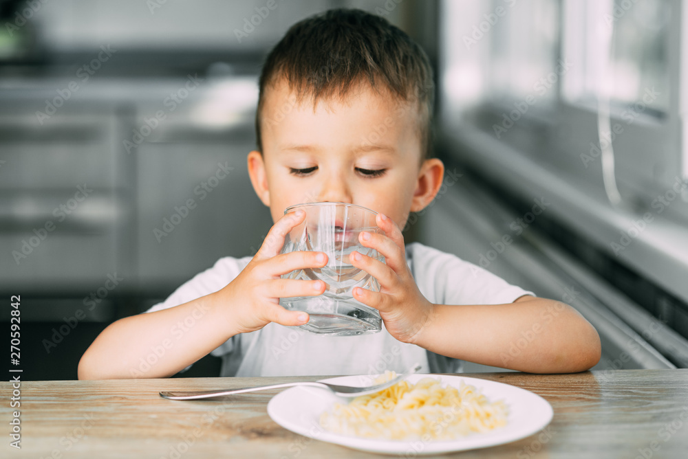 Boy in the kitchen drinking water from a glass, next to a plate of ...